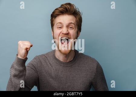 White ginger man with beard making handset gesture isolated over blue ...
