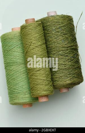 Different shades of green sewing threads on yellow background, flat lay ...