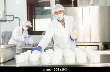 Cheesemaker in protective mask working in shaping workshop of cheese ...
