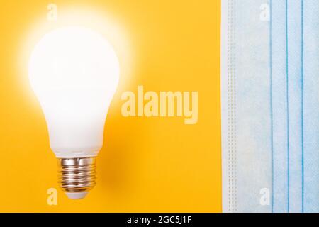 Glowing Power Saving Lamp with Medical Face Mask Lying on Yellow ...