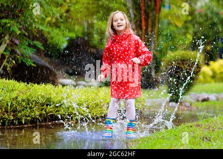 Child playing in puddle. Kids play and jump outdoor by autumn rain ...