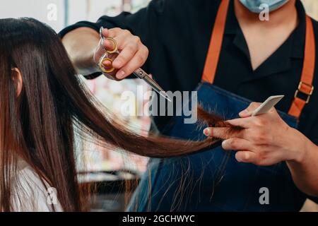 Young male hairdresser in mask cuts hair of girl in mask at beauty ...