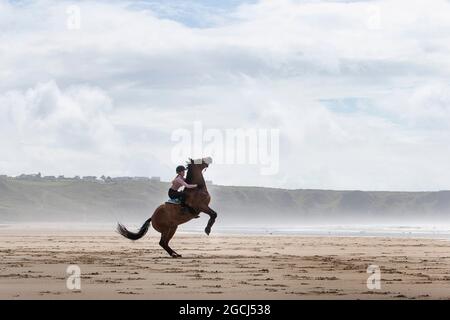 Women ride horse on Rhossilli Bay beach in West Wales, UK with the haze ...