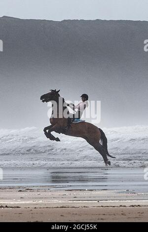Women ride horse on Rhossilli Bay beach in West Wales, UK with the haze ...