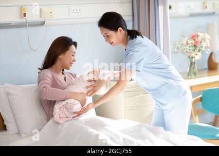Female nurse handing newborn baby to mother in hospital ward Stock ...
