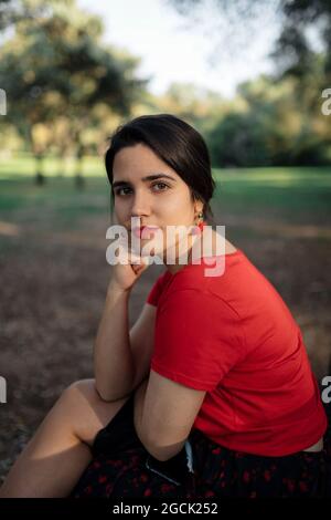 Side view of charming female chilling on bench and looking at camera ...