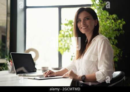 Beautiful Female Data Analyst sitting at the Table Works on a Laptop ...