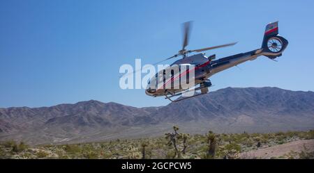 A helicopter is flying over a desert landscape with a large mountain in ...