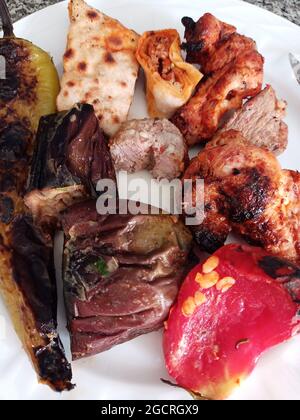 Top view of barbequed vegetables and meat on a white plate with cutlery ...