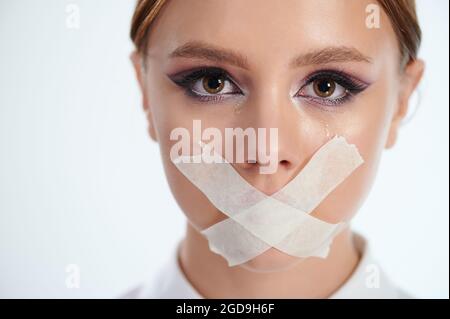 Young woman with taped mouth on dark background. Censorship concept ...