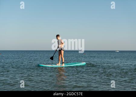 A 12 year old boy learns to stand on a SUP board in the sea near the ...