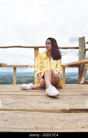 A woman sitting on a wooden platform by a pond in the park in summer ...