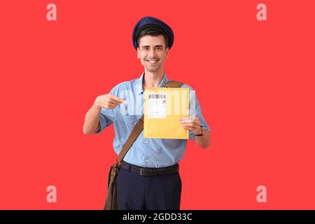 Handsome young postman pointing at letter on color background Stock ...