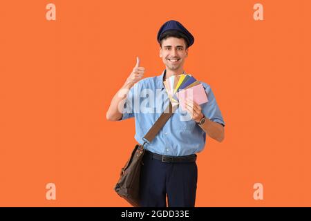 Handsome young postman with letters showing thumb-up on color ...