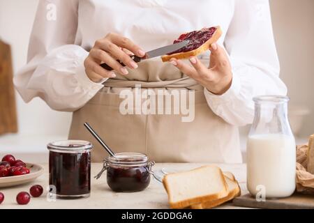 Woman spreading tasty cherry jam onto bread in kitchen Stock Photo - Alamy