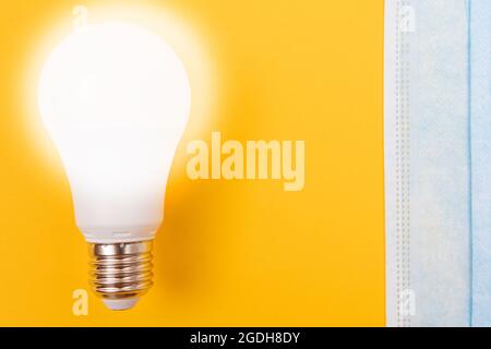 Glowing Power Saving Lamp with Medical Face Mask Lying on Yellow ...
