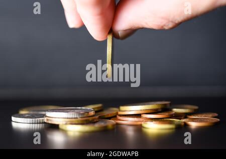 Hand drops a coin into a stack of coins on a black background Stock ...