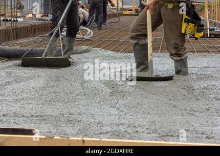 Workers leveling poured liquid concrete or cement on steel ...