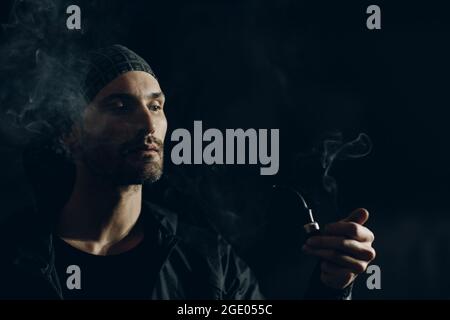Man smokes smoking pipe against dark background. Back side lit profile ...