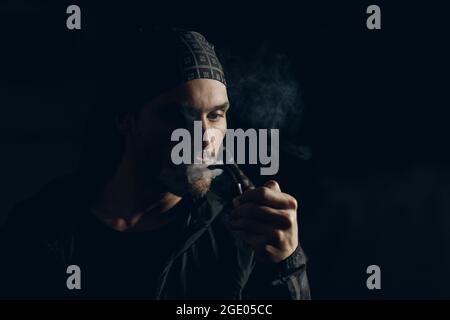 Man smokes smoking pipe against dark background. Back side lit profile ...