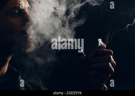 Man smokes smoking pipe against dark background. Back side lit profile ...