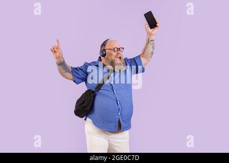 cheerful plus size man with mobile phone and wireless earphones ...