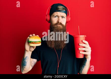 Redhead man with long beard eating a tasty classic burger and drinking ...
