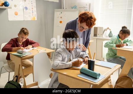 Youthful schoolboy bending over desk and covering his head by hands ...