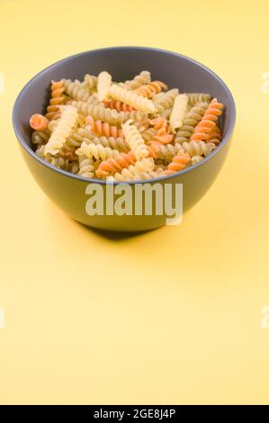 Vertical shot of tri-color rotini pasta on a bowl isolated on yellow ...