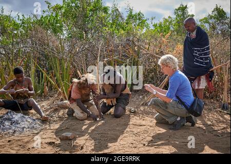 tourist watching bushmen making fire, bushmen of Hadzabe tribe sitting ...