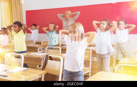 Teacher conducts gymnastics for elementary school children in classroom ...