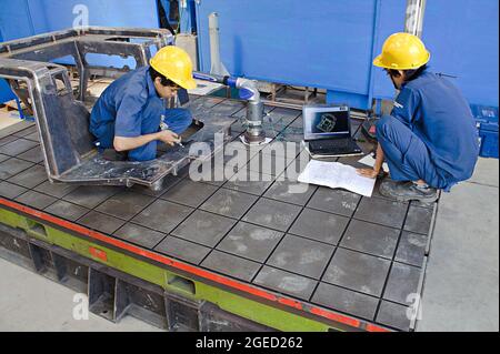 Two technicians use measurement tool and laptop in a metal fabrication ...