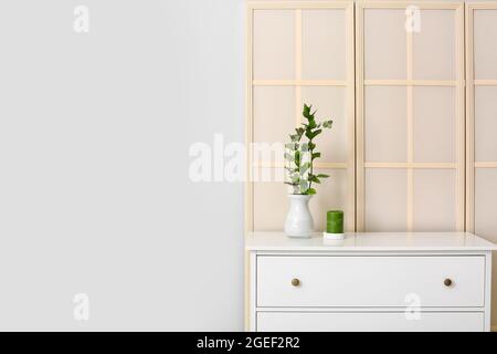 Chest of drawers with candle and eucalyptus branches near light wall ...