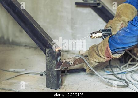 Man welder assembles a metal staircase structure in a residential ...