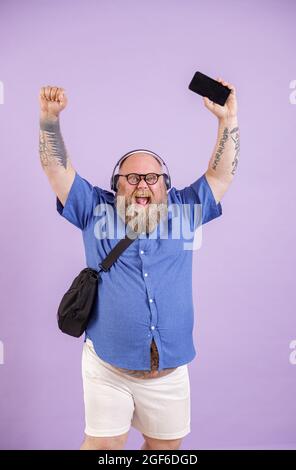 cheerful plus size man with mobile phone and wireless earphones ...