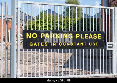 Large yellow and black sign on metal gate saying no parking please ...