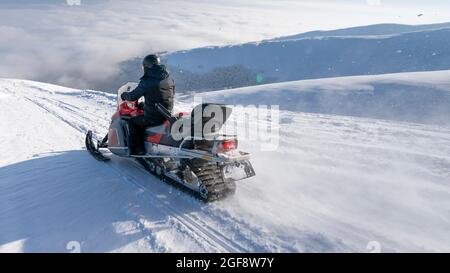 The snowmobile moves on the slope of a snow-capped mountain Stock Photo ...