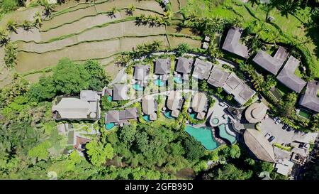 aerial view of luxury hotel with straw roof villas and pools in tropical jungle and palm trees ...