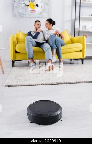 Robotic vacuum cleaner near blurred man talking on smartphone in living ...