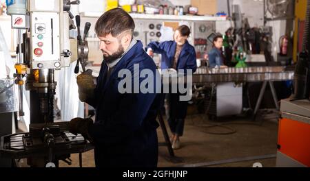 Workman drilling metal parts on stationary machine Stock Photo - Alamy