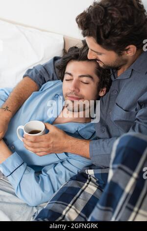 Positive and tattooed gay man hugging friends holding lgbt flags and ...