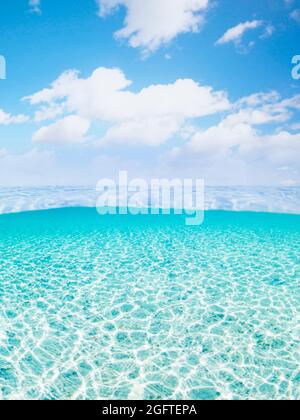 A split level shot of turquoise ocean water and clouds in a blue sky ...