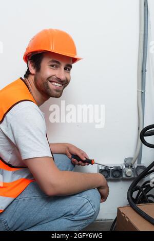 Handsome young man holding screwdriver wearing hardhat smiling happy ...