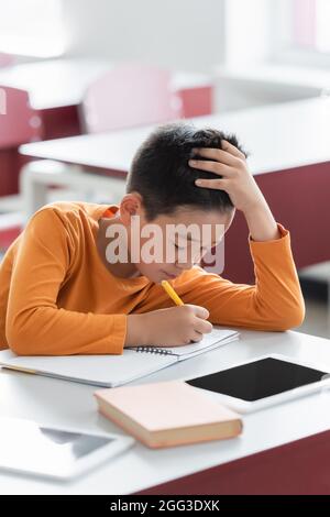 asian boy writing in notebook near blurred classmates Stock Photo - Alamy