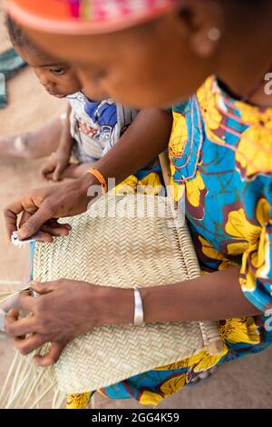 A Fulani woman weaves matts and fans from dried palm fronds by hand for ...