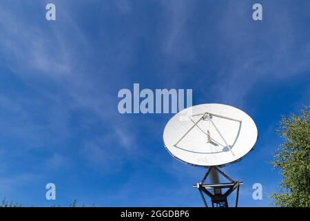 Big white satellite dish on a blue sky with tree branches in the ...