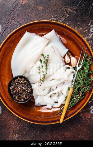 Sliced raw rings squid in a rustic plate with rosemary. Dark background ...