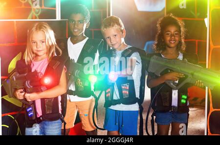 Joyful teens aiming laser guns at other players during lasertag game in ...