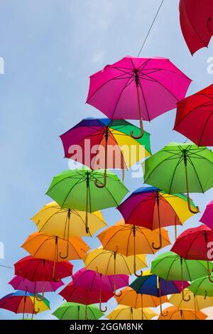 A low-angle shot of colorful umbrellas hanging from wires in an urban ...