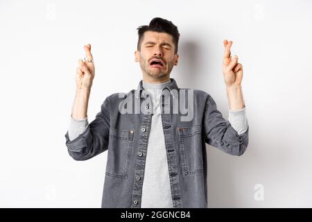 Sad and miserable man hoping god, cross fingers and crying, praying or ...